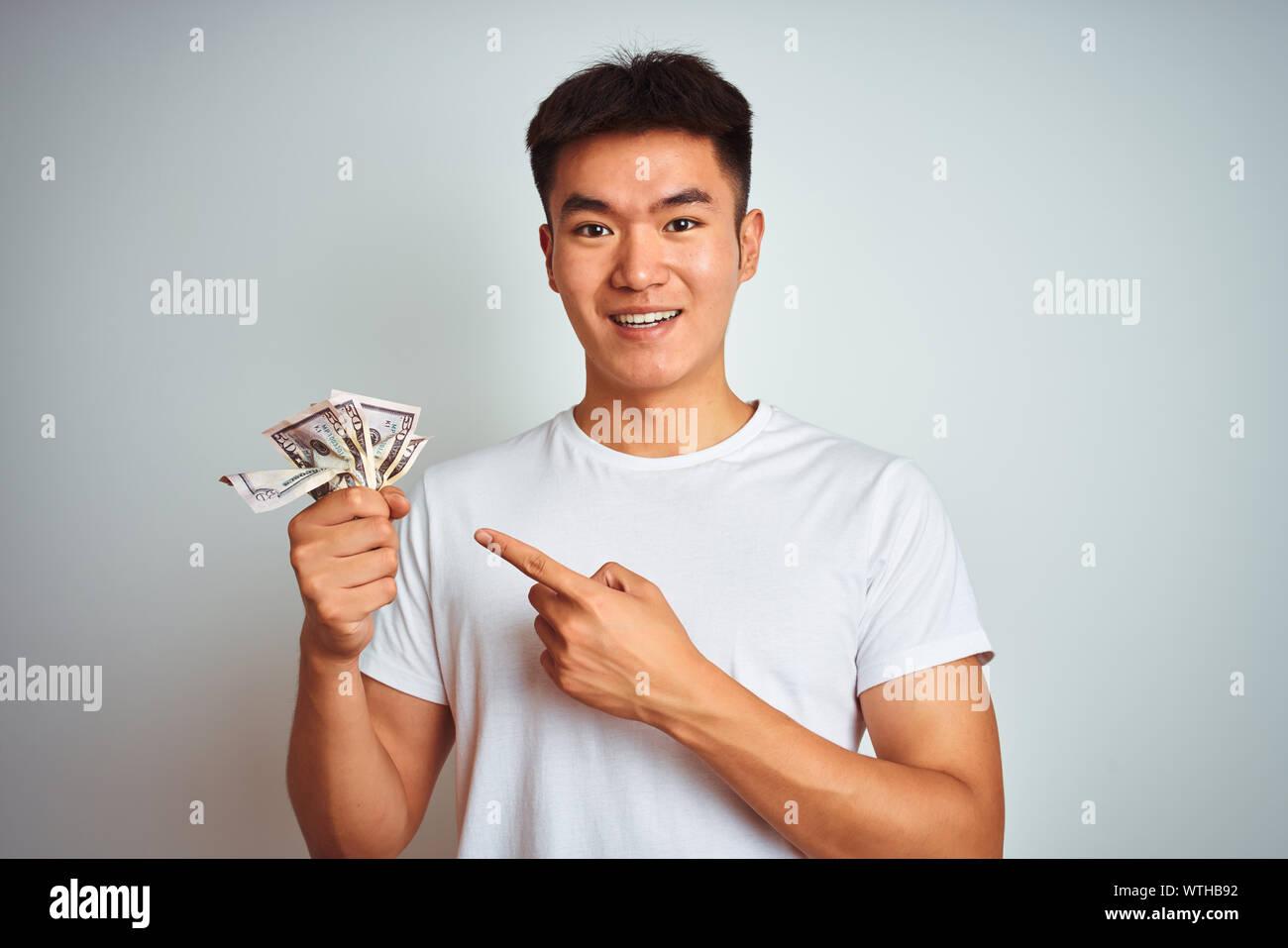 Young asian chinese man holding dollars standing over isolated white ...