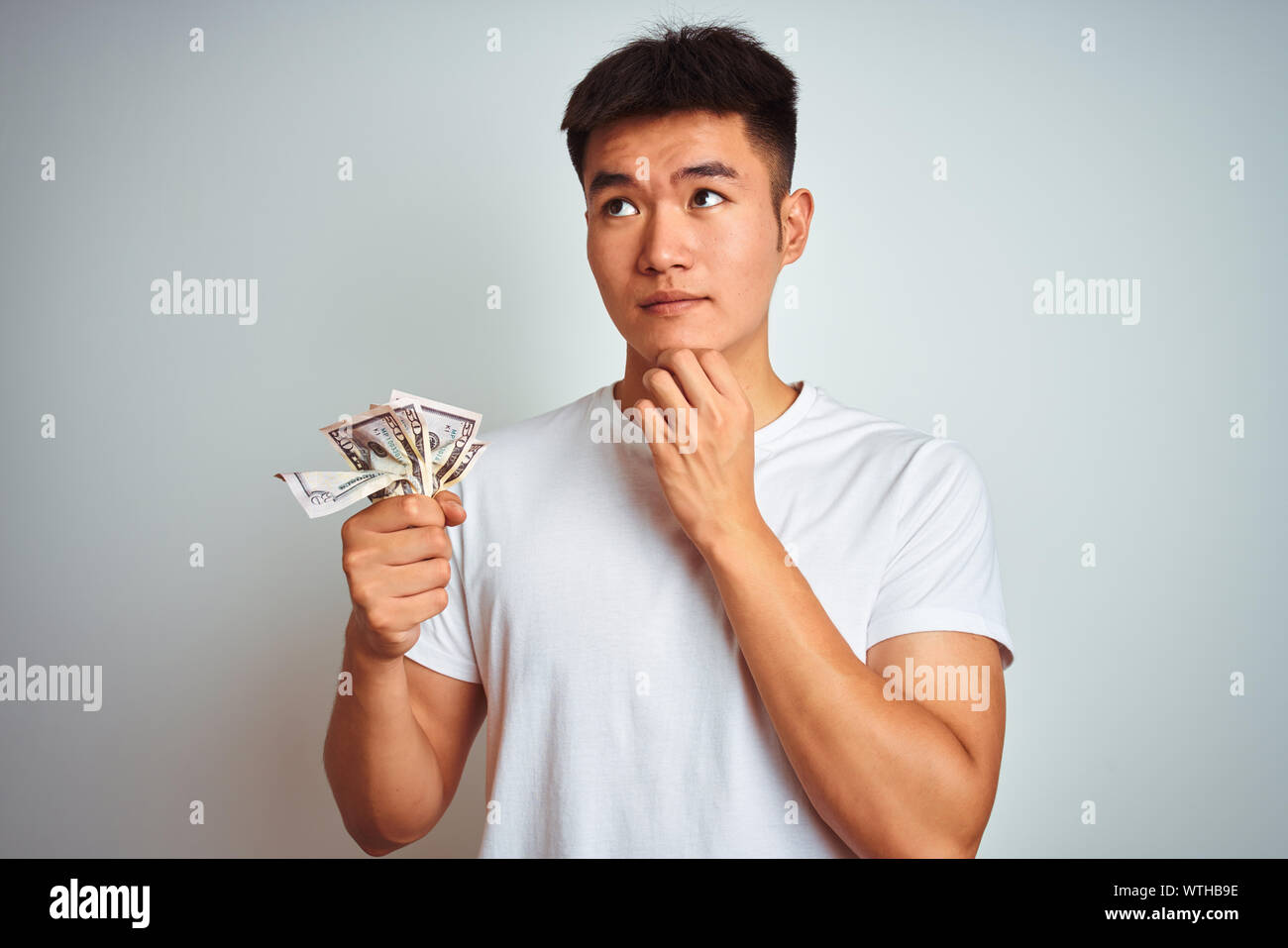 Young asian chinese man holding dollars standing over isolated white ...