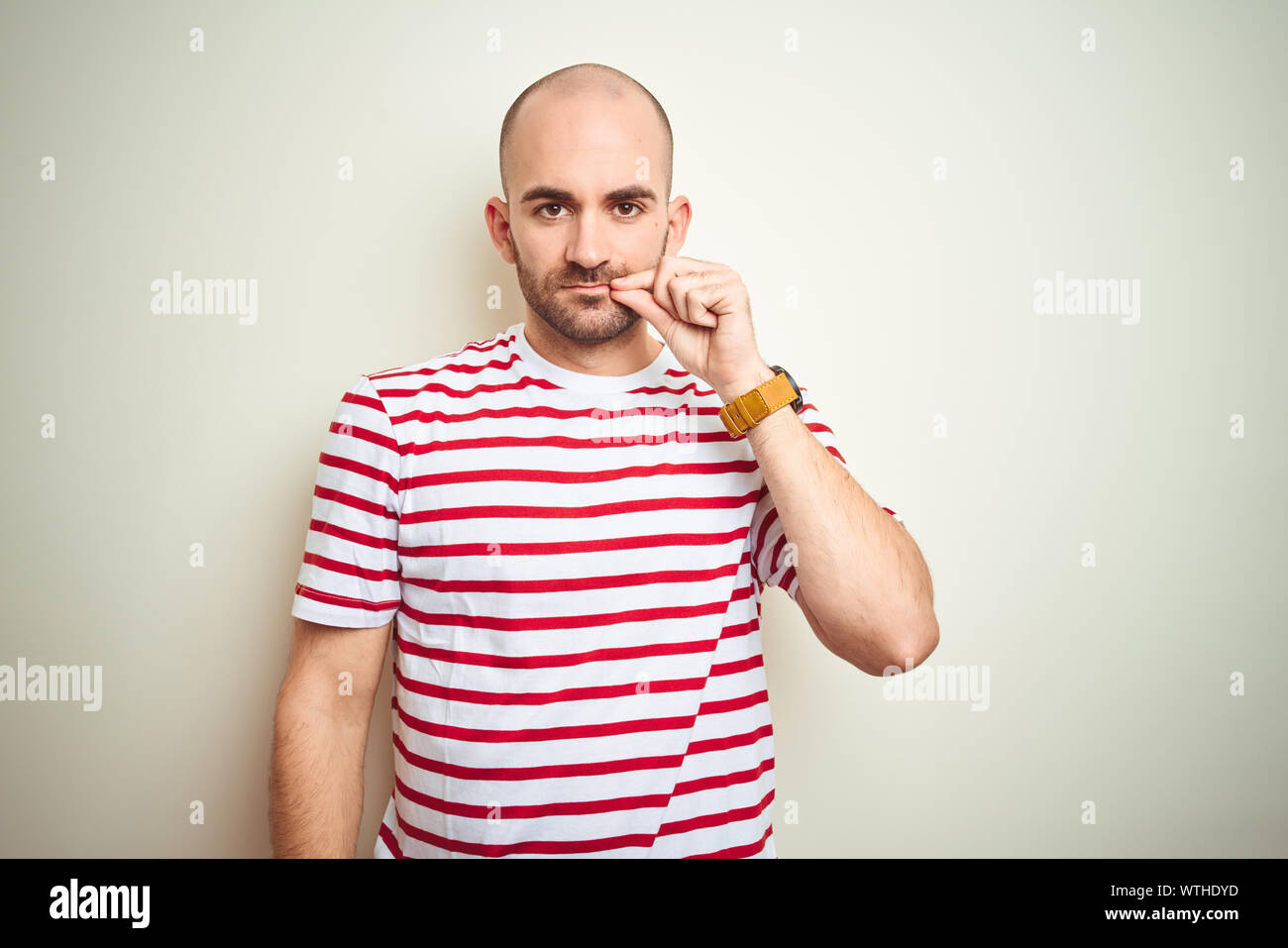 Young bald man with beard wearing casual striped red t-shirt over white ...