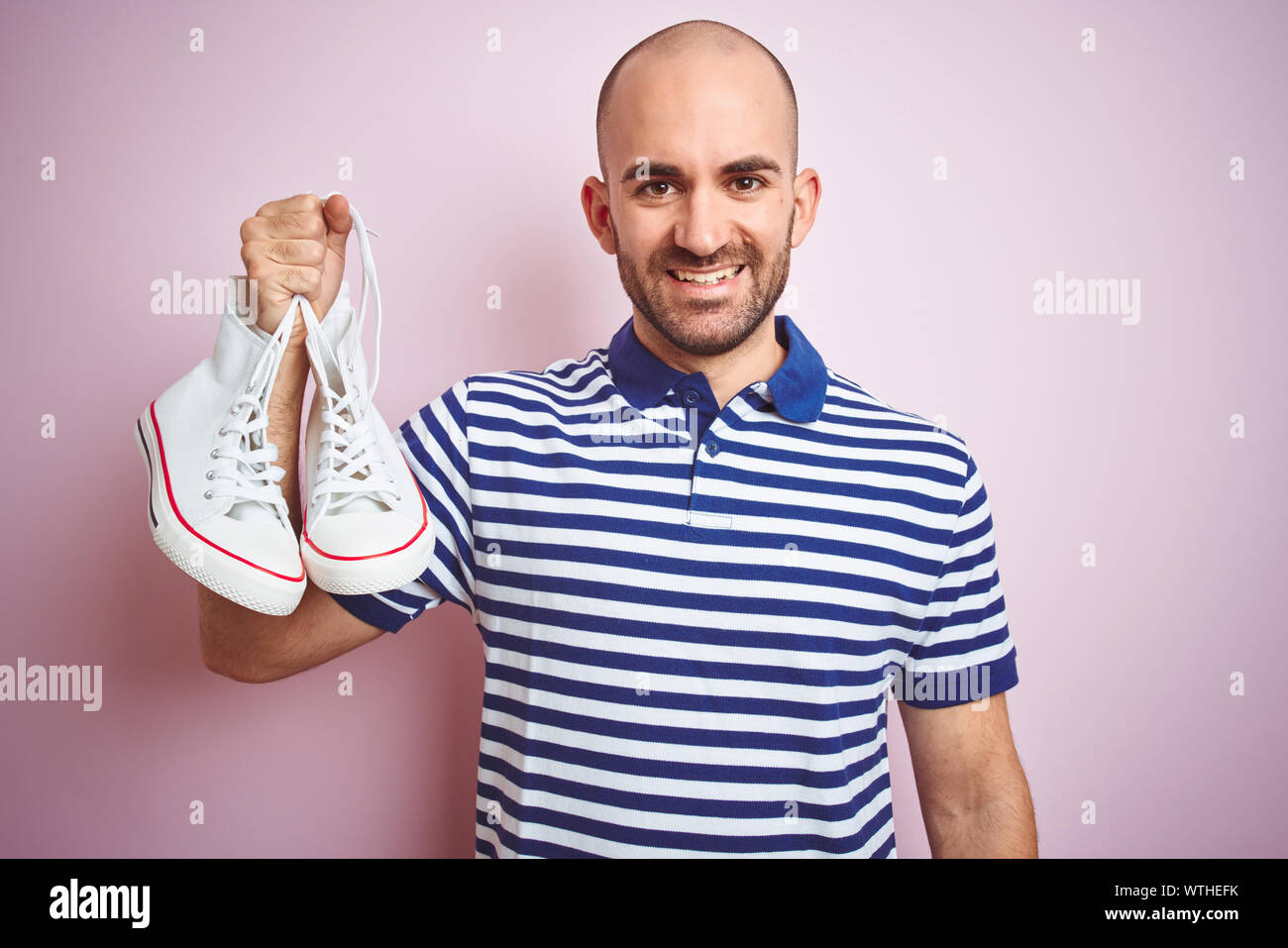 Young man holding casual sneakers shoes over pink isolated background ...