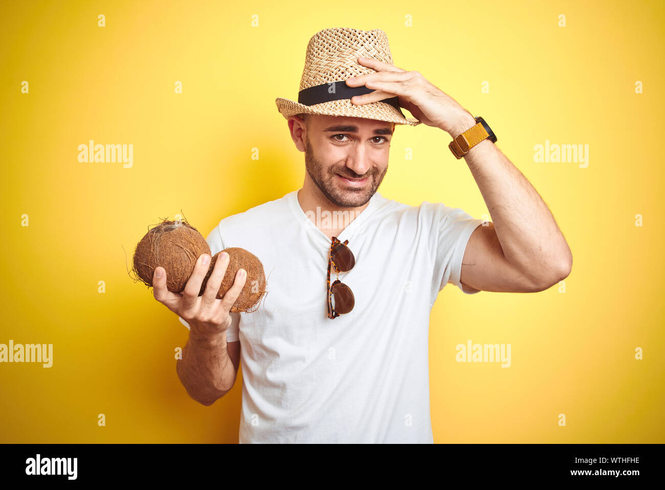 Young man wearing summer hat and holding coconut fruit over yellow ...