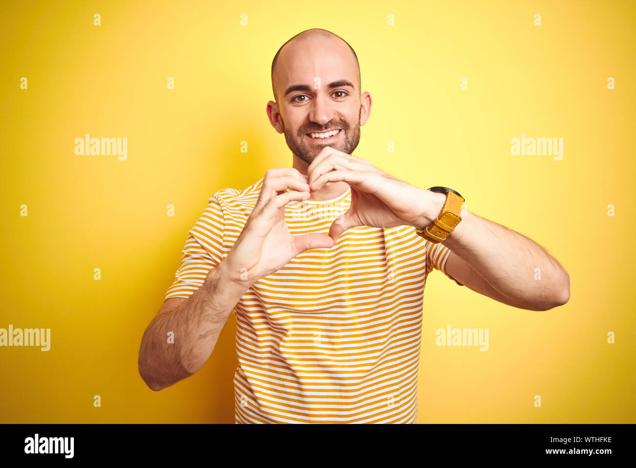 Young bald man with beard wearing casual striped t-shirt over yellow ...