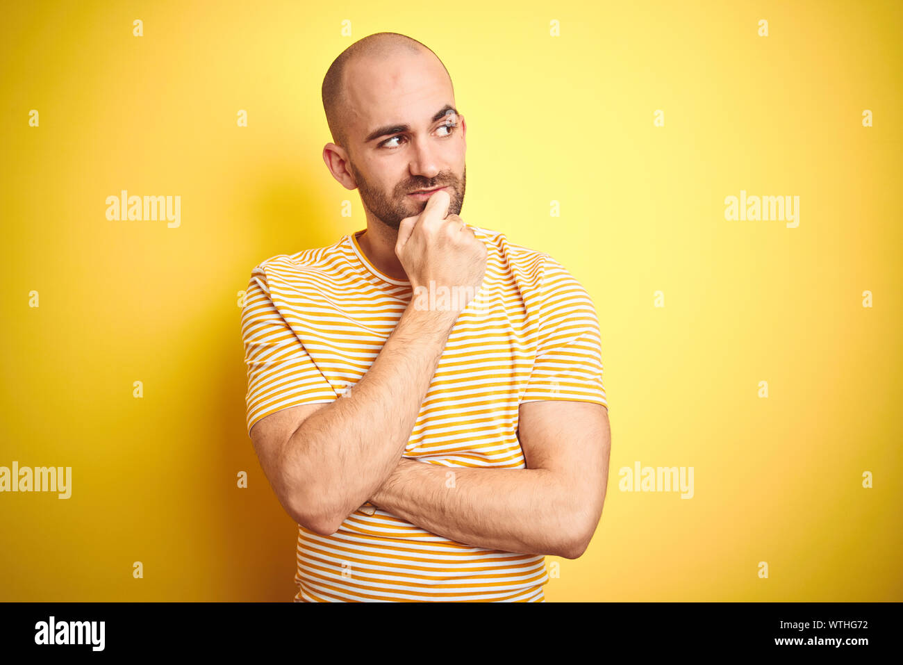 Young bald man with beard wearing casual striped t-shirt over yellow ...