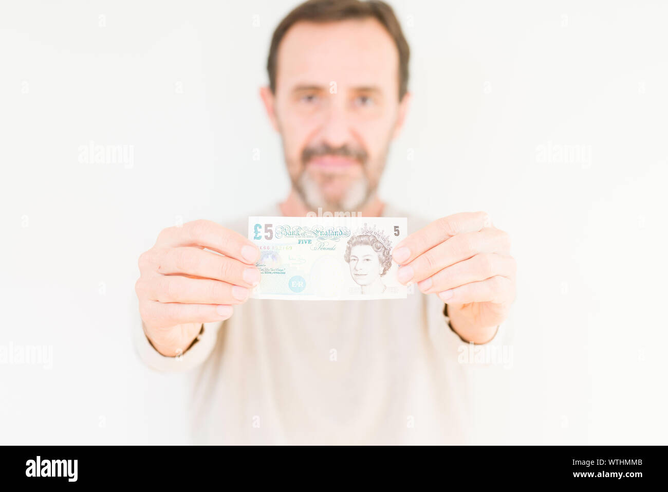 Senior man holding five pounds bank note over isolated background with ...