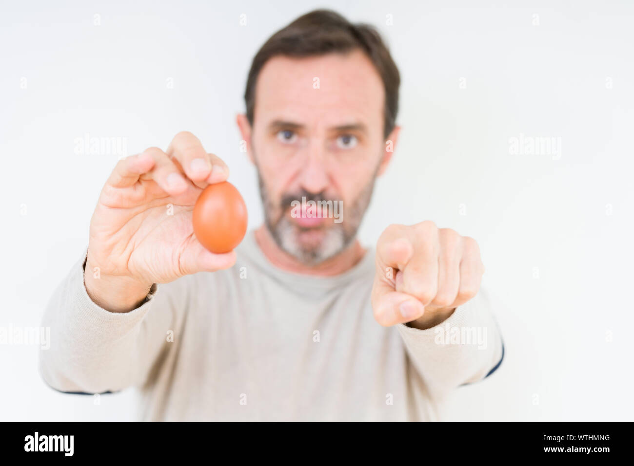 Senior man holding fresh egg over isolated background pointing with ...