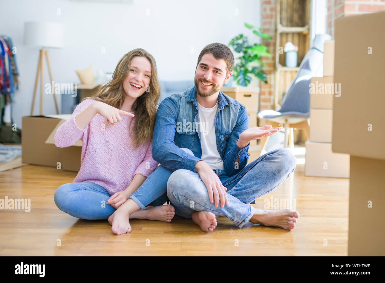 Young beautiful couple moving to a new house sitting on the floor ...