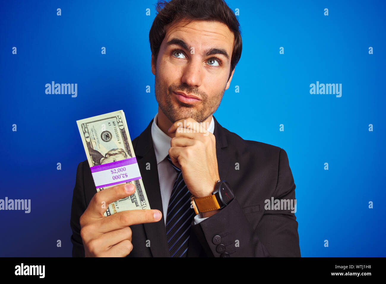 Young handsome businessman wearing suit holding dollars over isolated ...