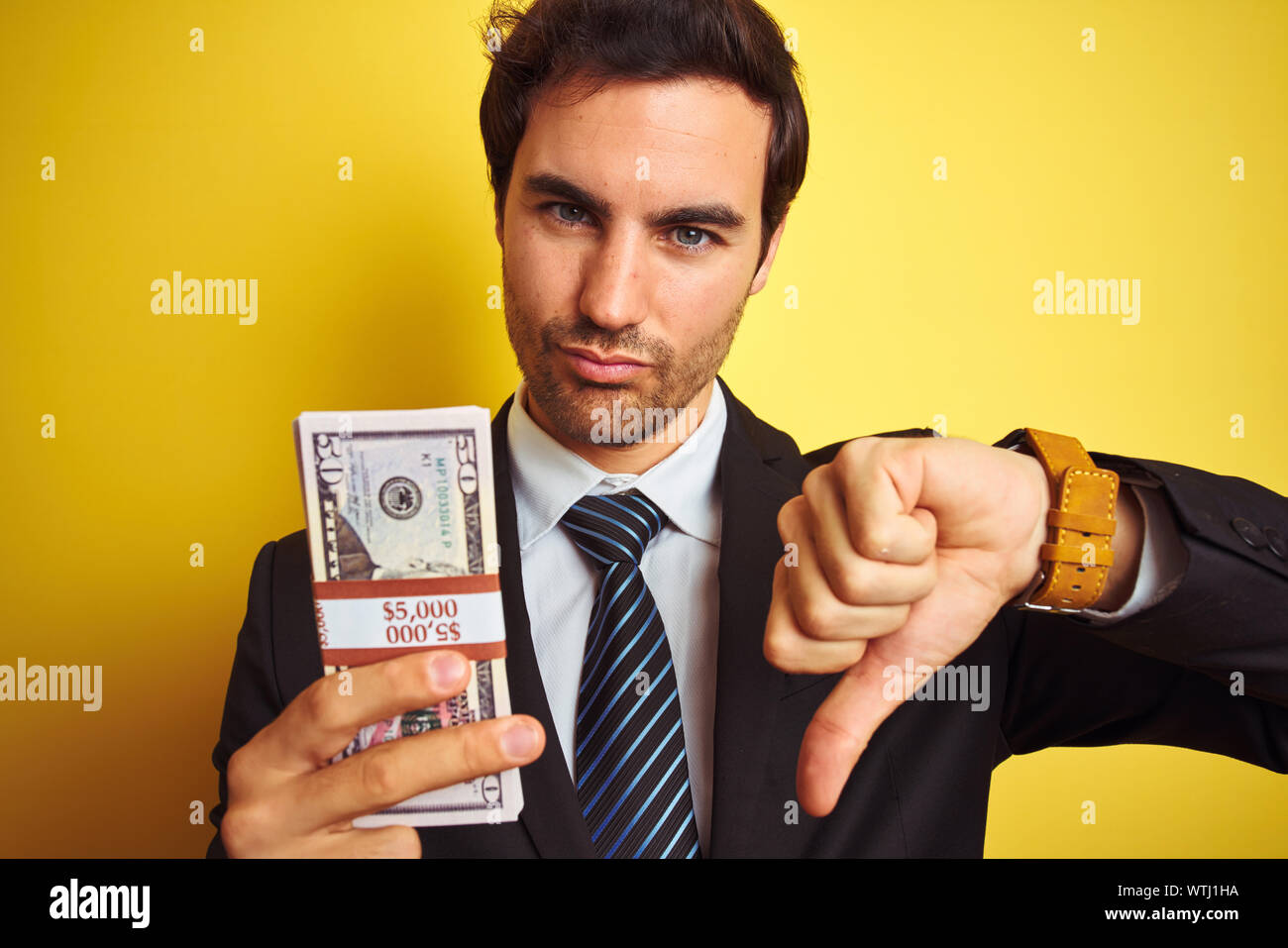 Young handsome businessman wearing suit holding dollars over isolated ...