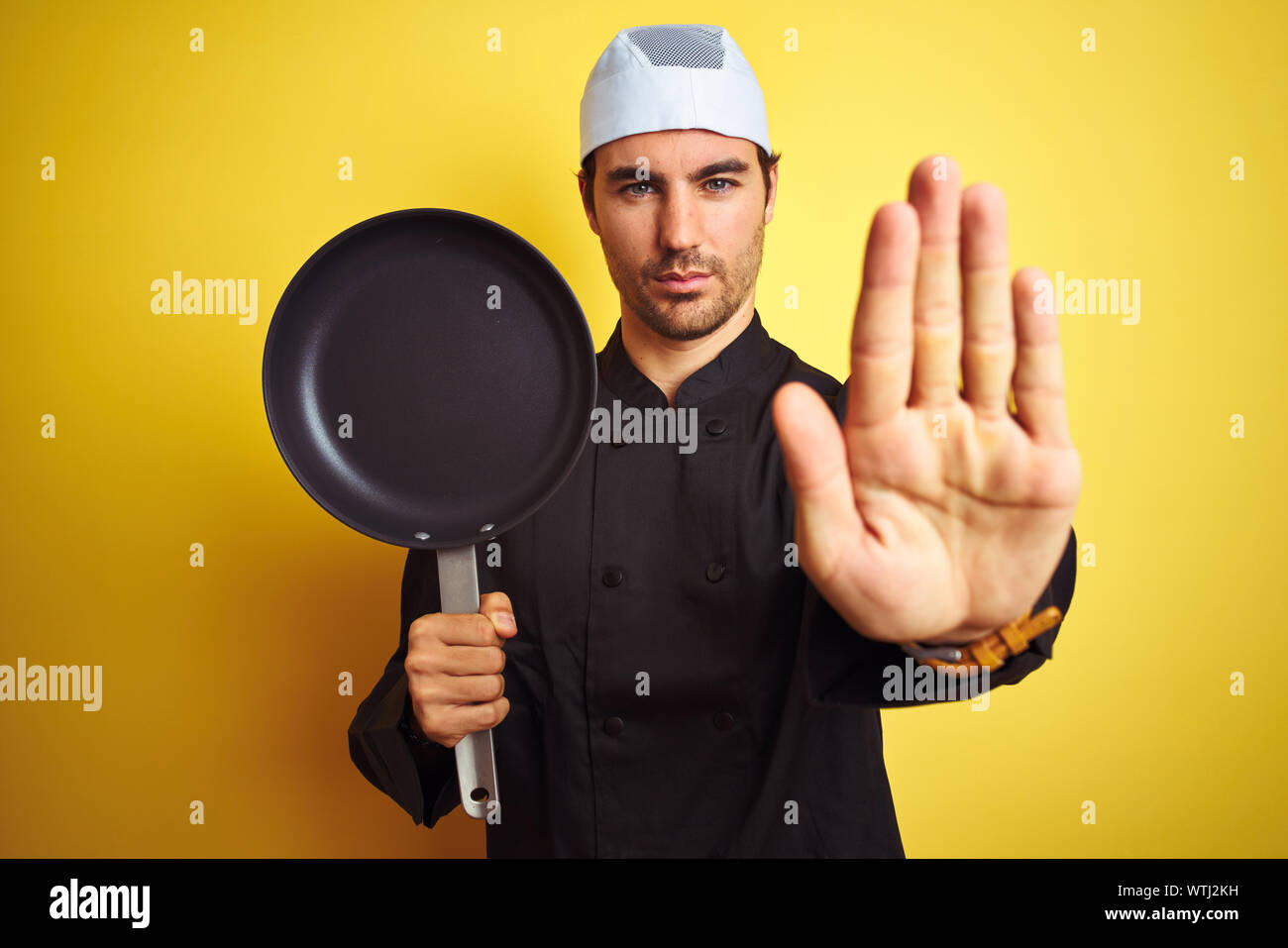 Young chef man wearing uniform and hat holding cook pan over isolated ...