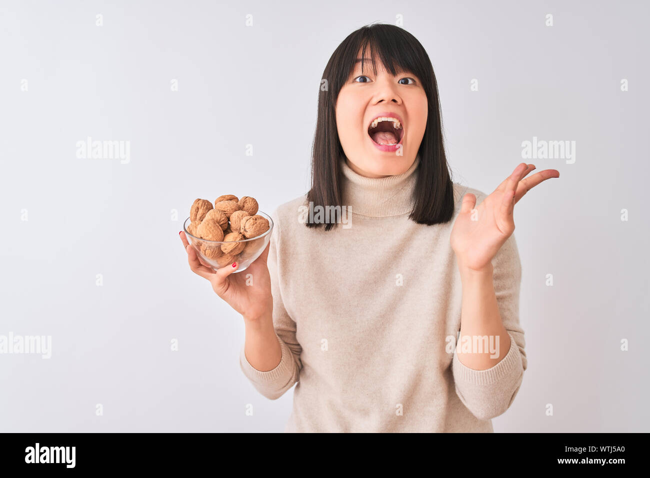 Young beautiful Chinese woman holding bowl with walnuts over isolated ...