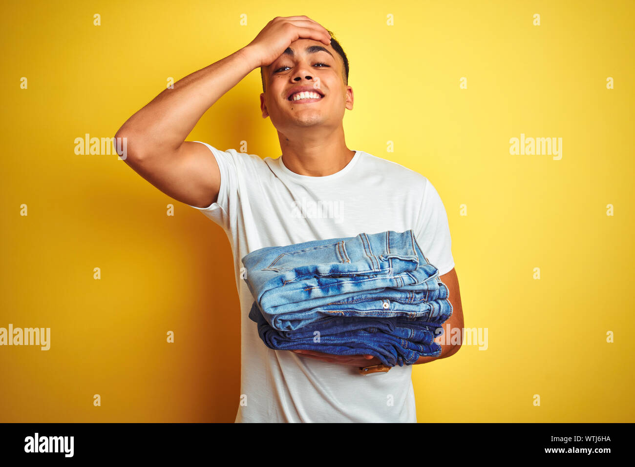 Young brazilian shopkeeper man holding jeans standing over isolated ...