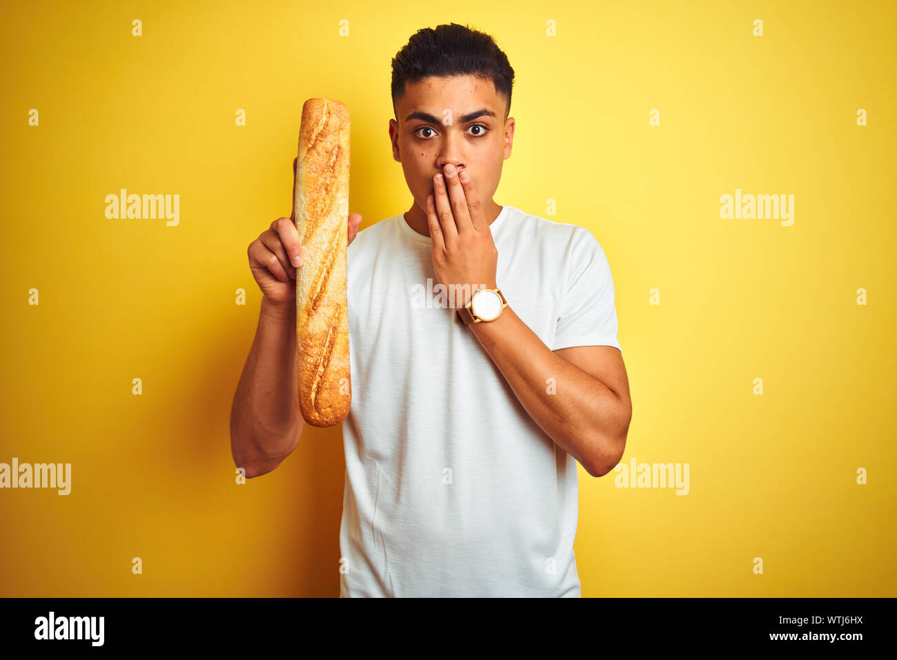 Young brazilian baker man holding bread standing over isolated yellow ...