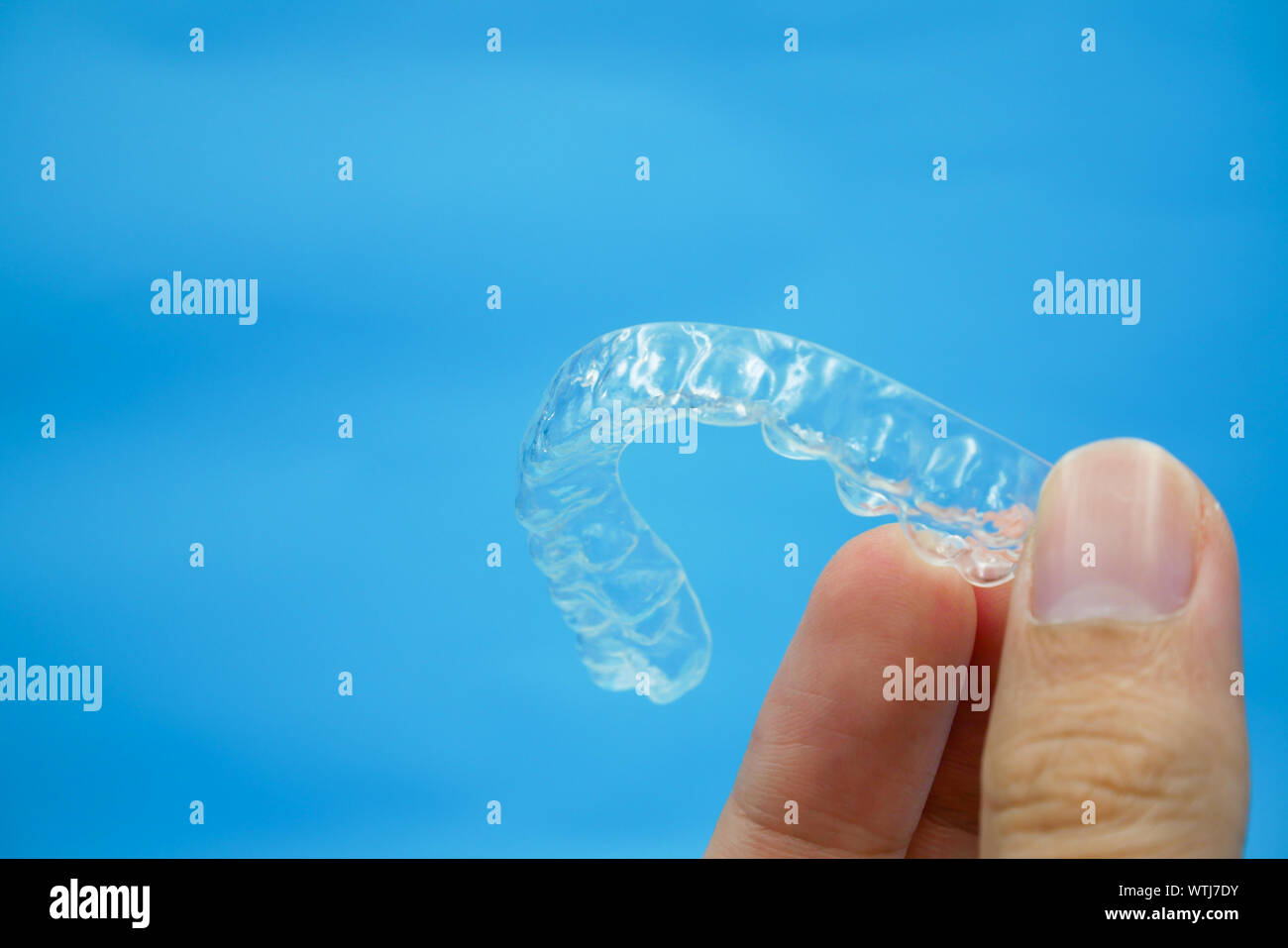 hand holding clear plastic retainer teeth that isolated on blue sky ...
