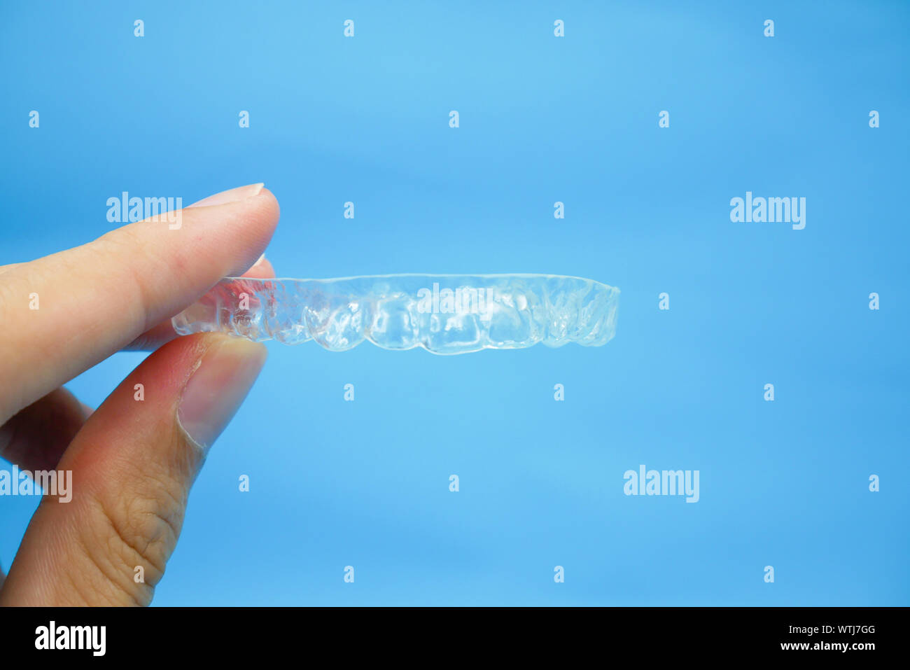 hand holding clear plastic retainer teeth that isolated on blue sky ...