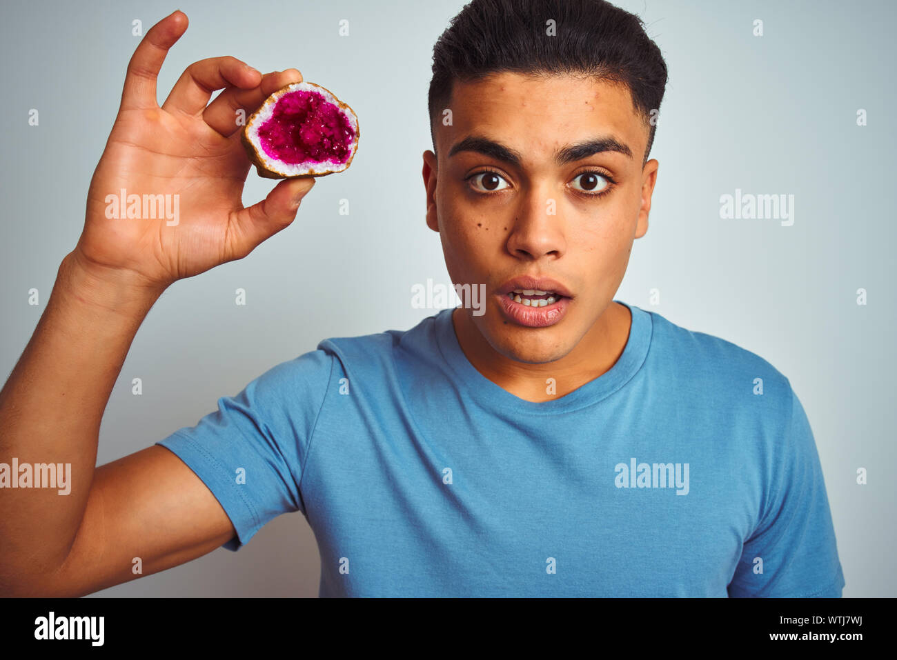 Young brazilian man holding amethyst gemstone standing over isolated ...