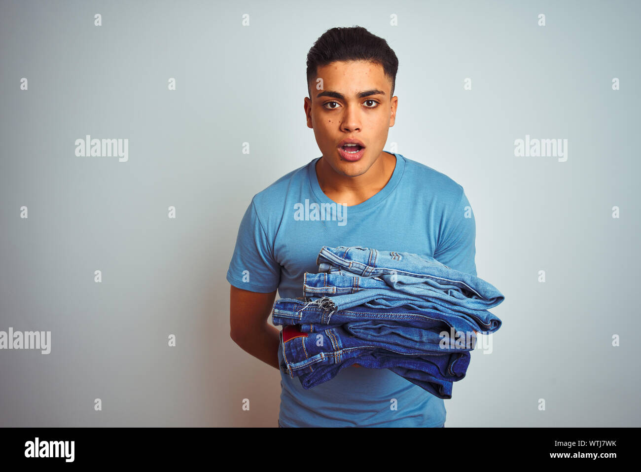 Young brazilian shopkeeper man holding jeans standing over isolated ...