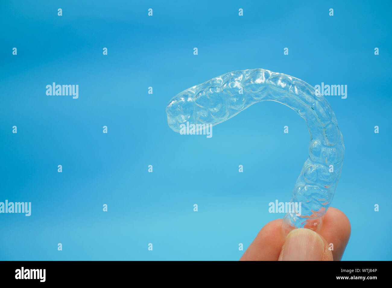 hand holding clear plastic retainer teeth that isolated on blue sky ...