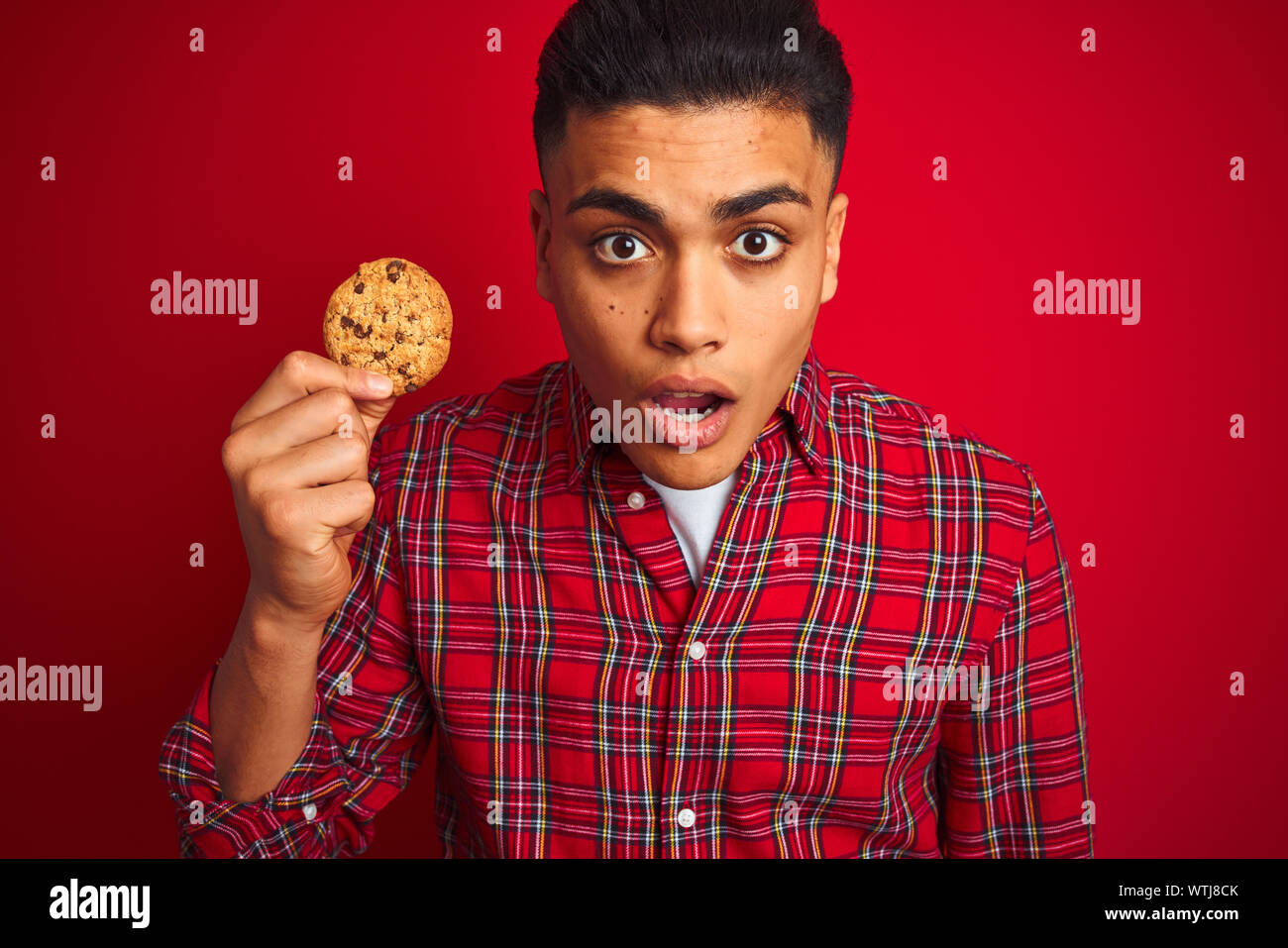 Young brazilian man holding a cookie standing over isolated red ...