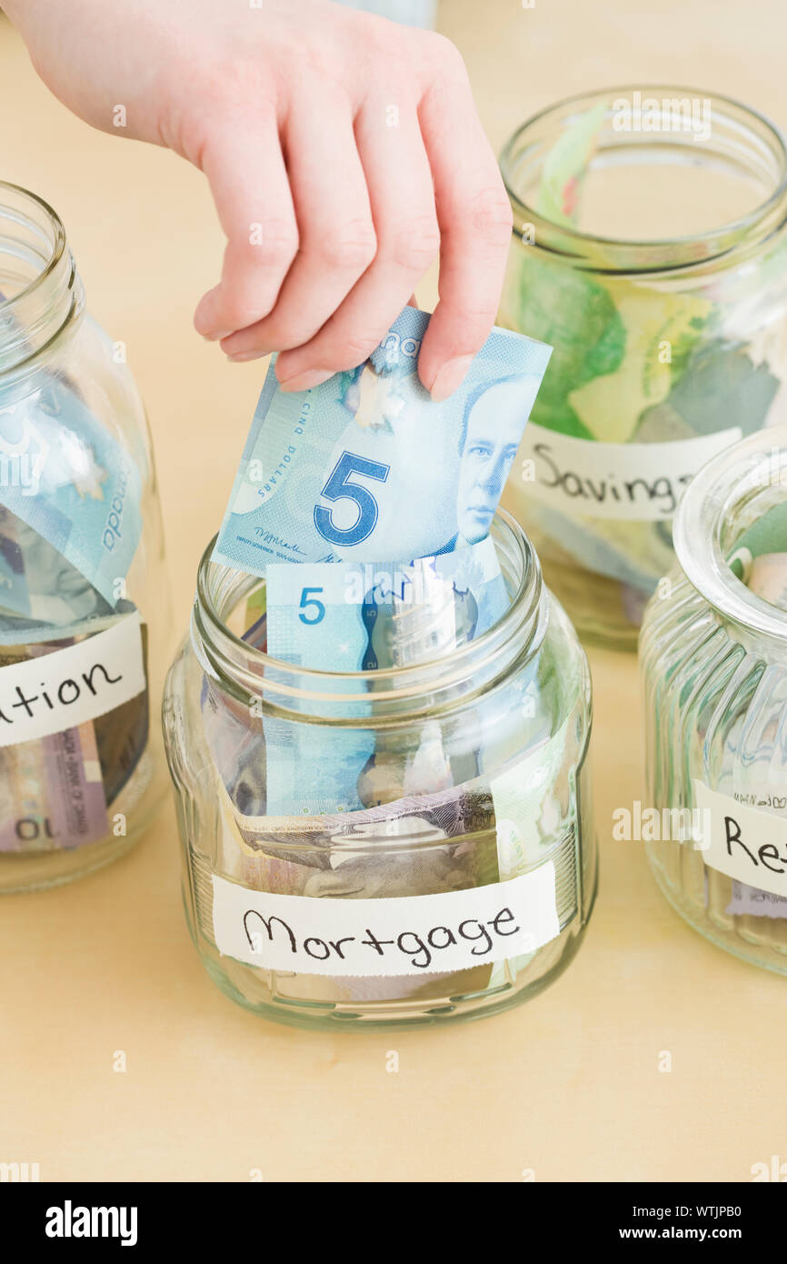Teenage girl's (16-17) hand filling jar with mortgage label with ...