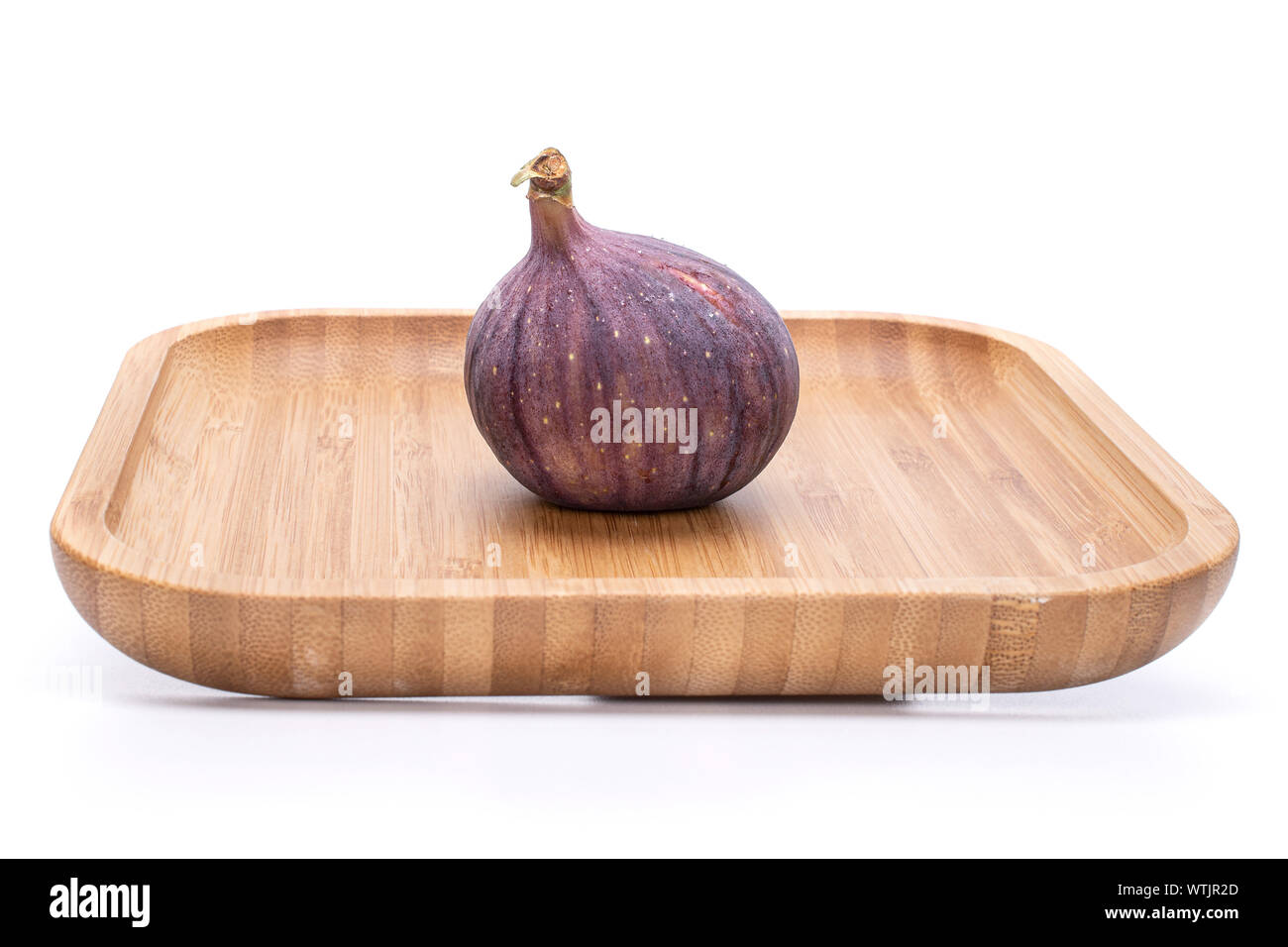 One whole fresh fig fruit on bamboo plate isolated on white background ...