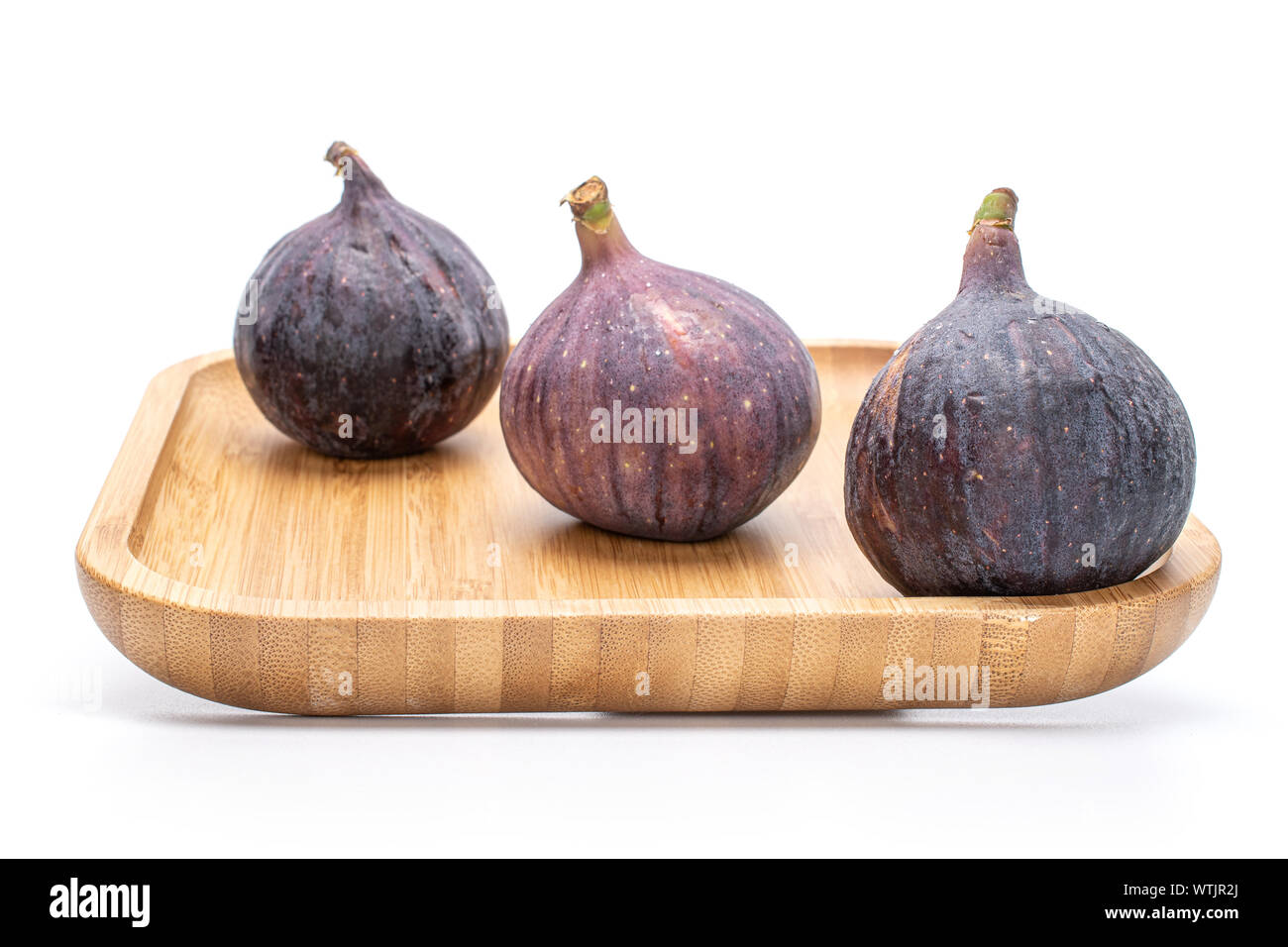 Group of three whole fresh fig fruit on bamboo plate isolated on white ...