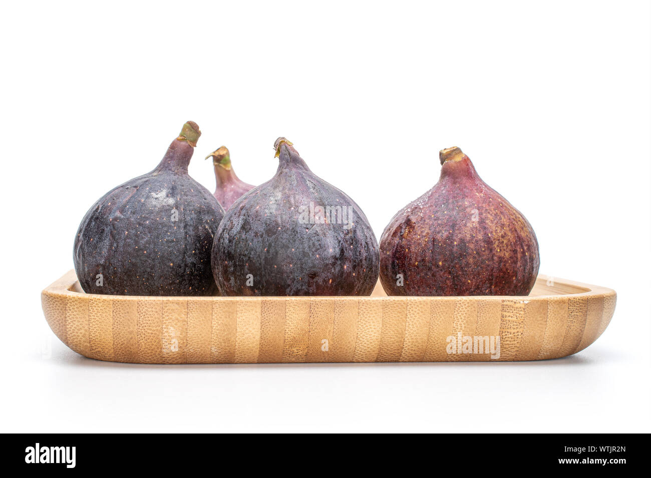 Group of four whole fresh fig fruit on bamboo plate isolated on white ...