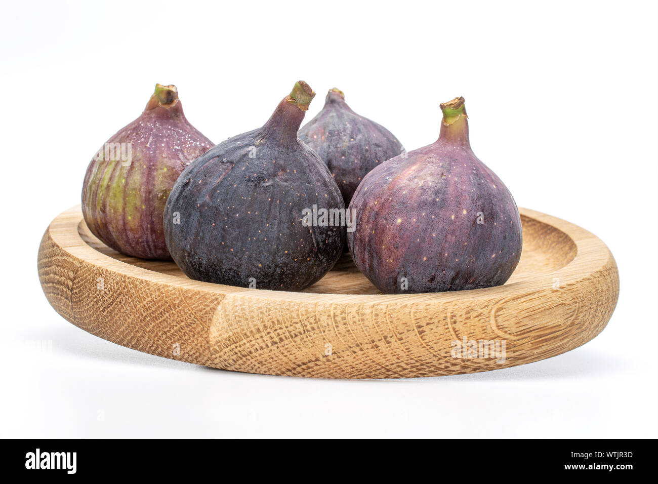 Group of four whole velvety fresh fig fruit on bamboo plate isolated on ...
