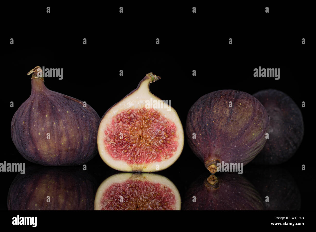 Group of two whole one half of fresh fig fruit isolated on black glass ...