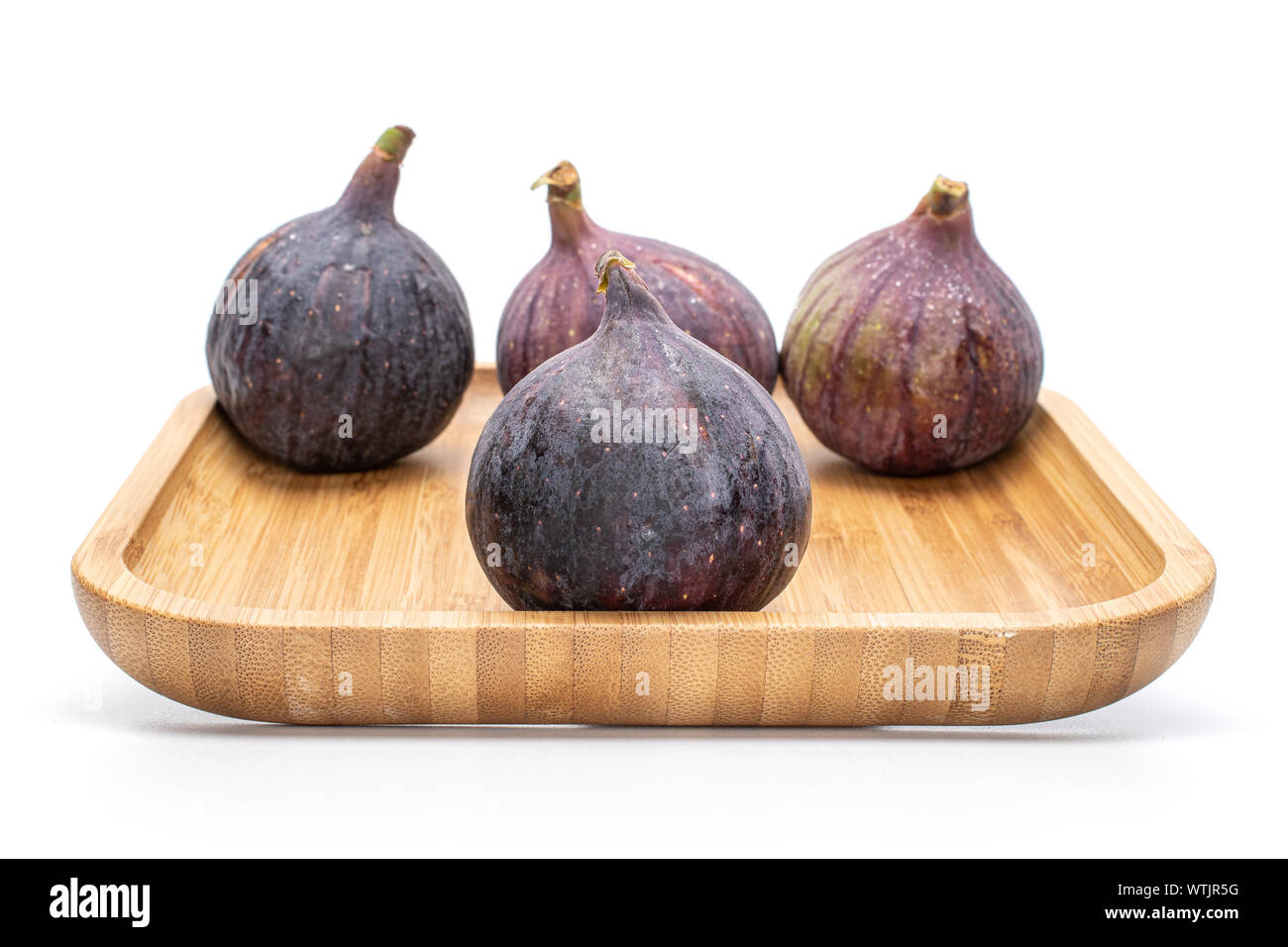 Group of four whole fresh fig fruit on bamboo plate isolated on white ...
