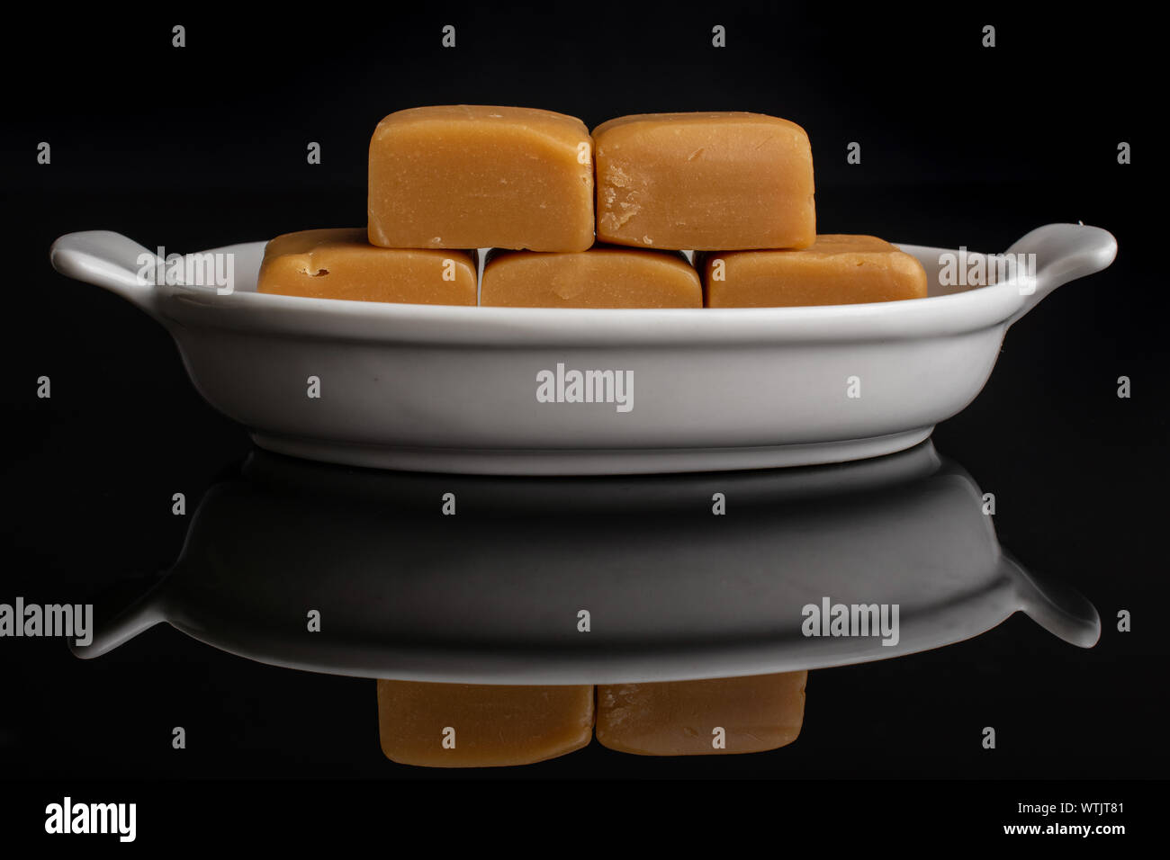 Group of five whole sweet golden caramel candy in white oval ceramic ...