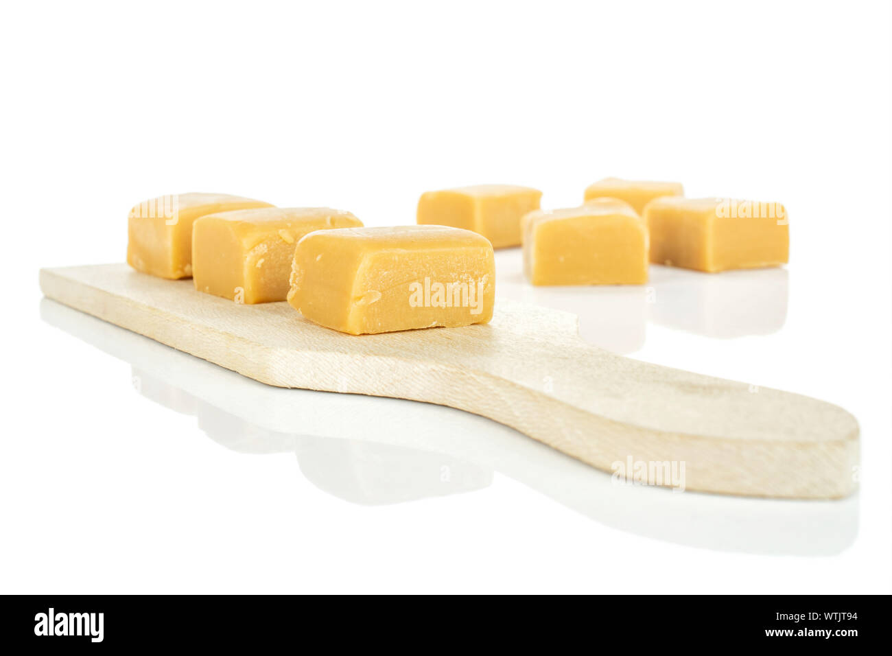 Group of seven whole sweet golden caramel candy on small wooden cutting ...