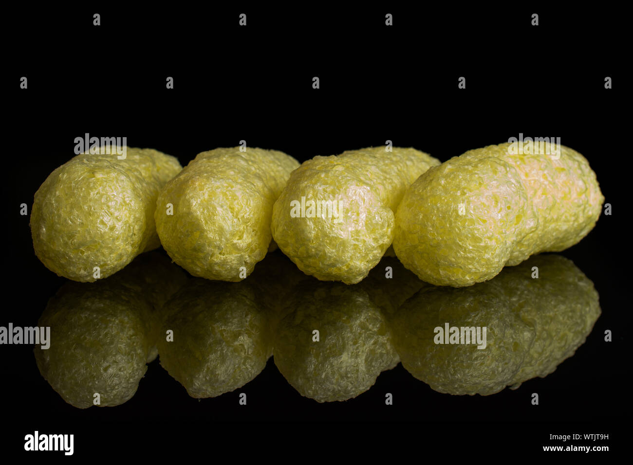 Group of four whole salted yellow corn puff isolated on black glass ...