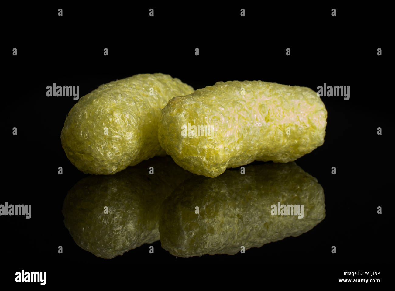 Group of two whole salted yellow corn puff isolated on black glass ...