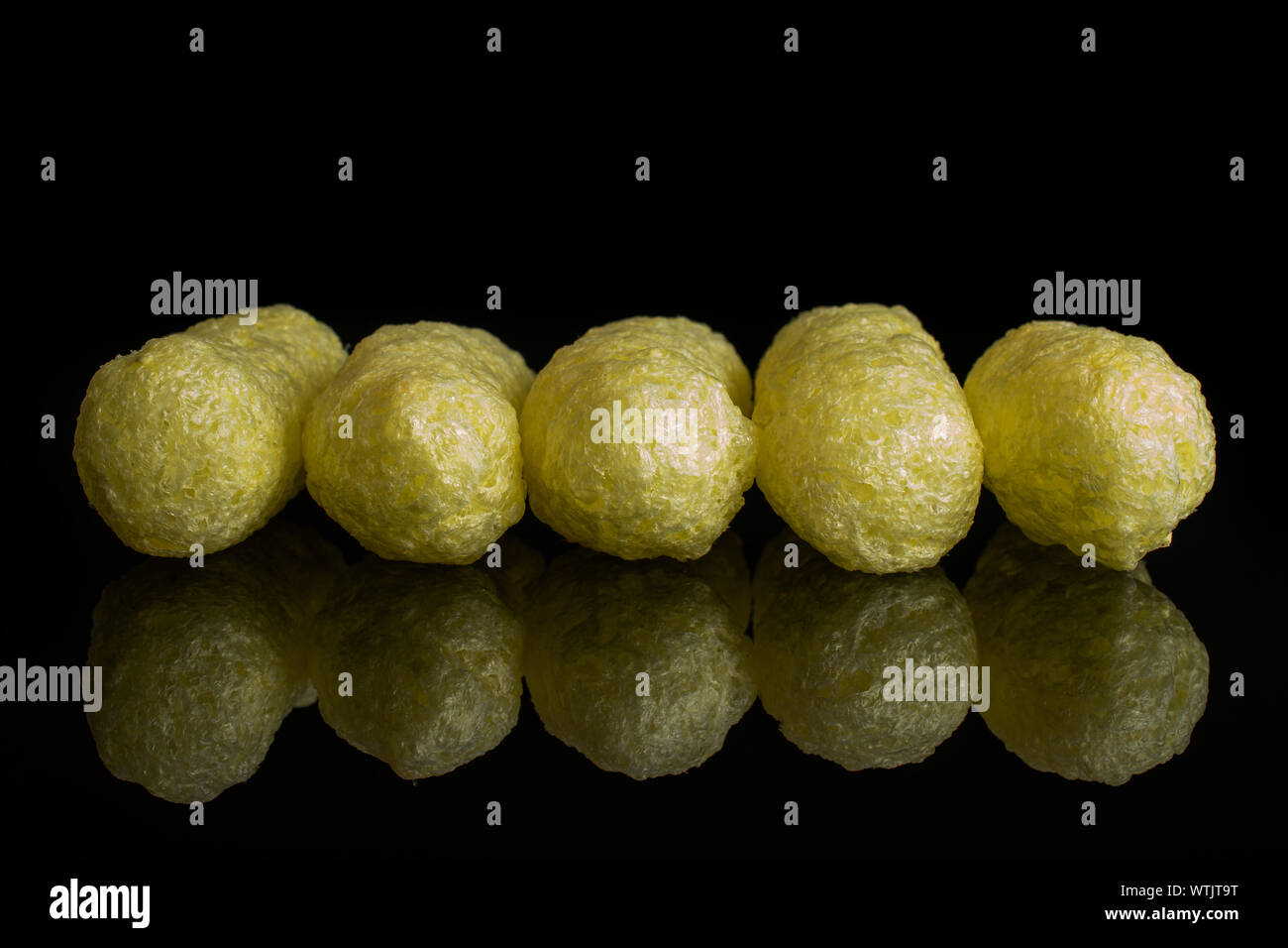 Group of five whole salted yellow corn puff isolated on black glass ...