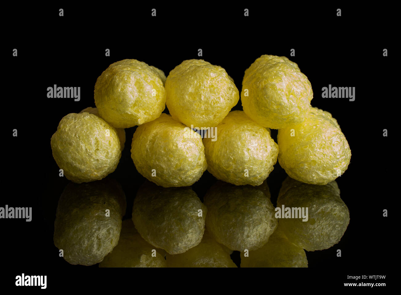 Group of seven whole salted yellow corn puff isolated on black glass ...