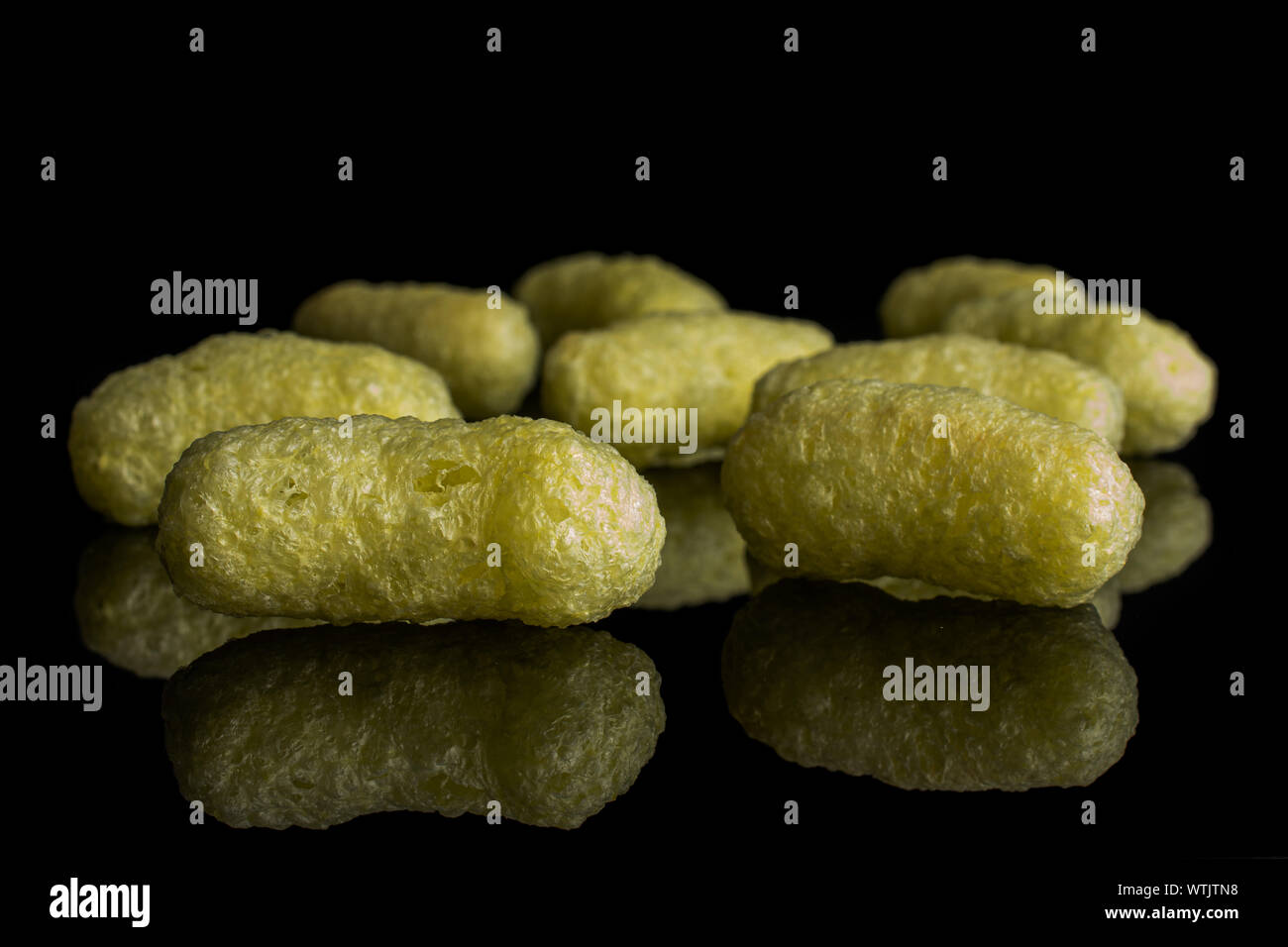 Group of nine whole salted yellow corn puff isolated on black glass ...