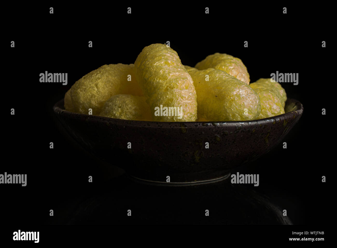 Lot of whole salted yellow corn puff in dark ceramic bowl isolated on ...