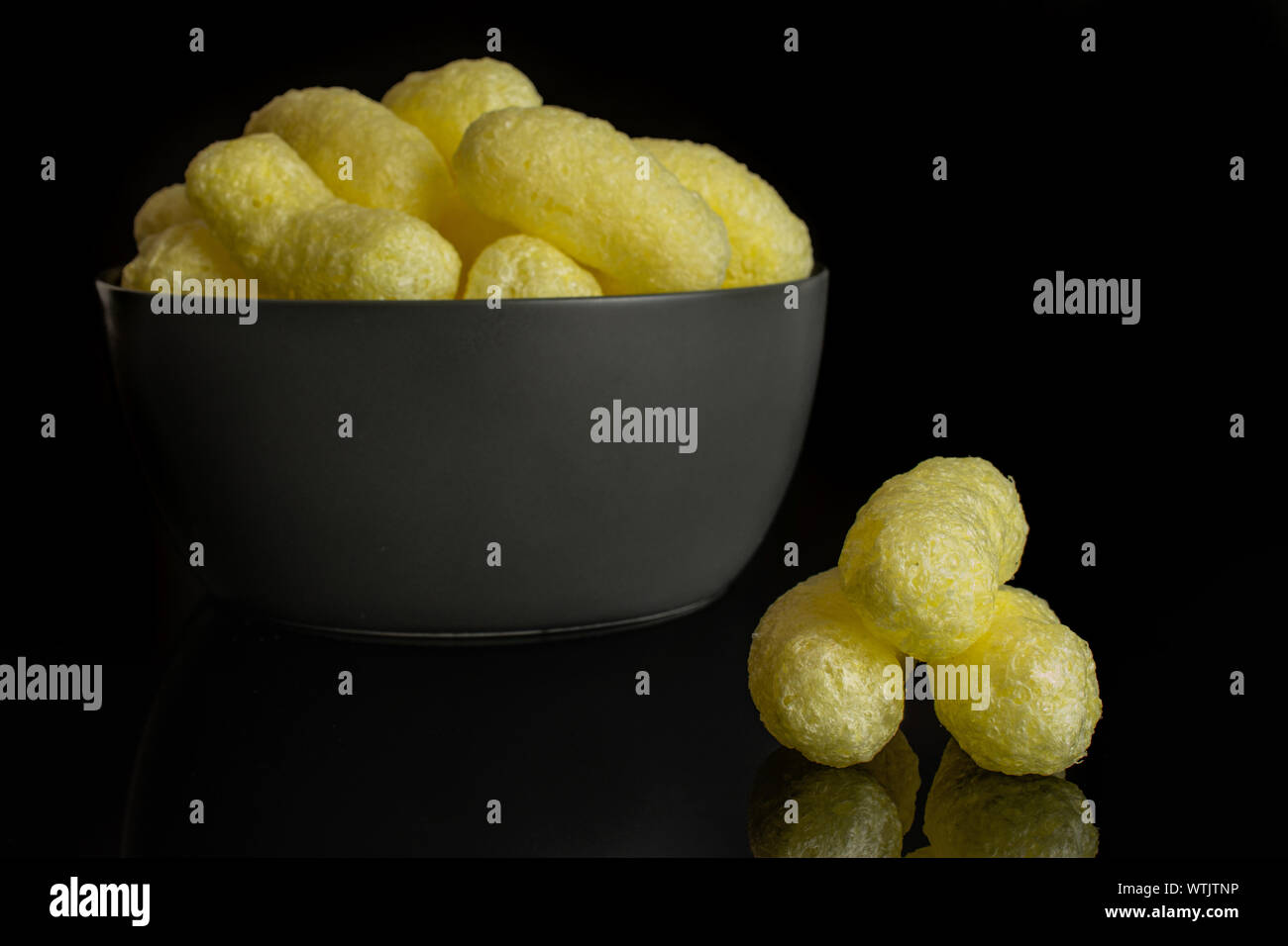 Lot of whole salted yellow corn puff in gray ceramic bowl isolated on ...