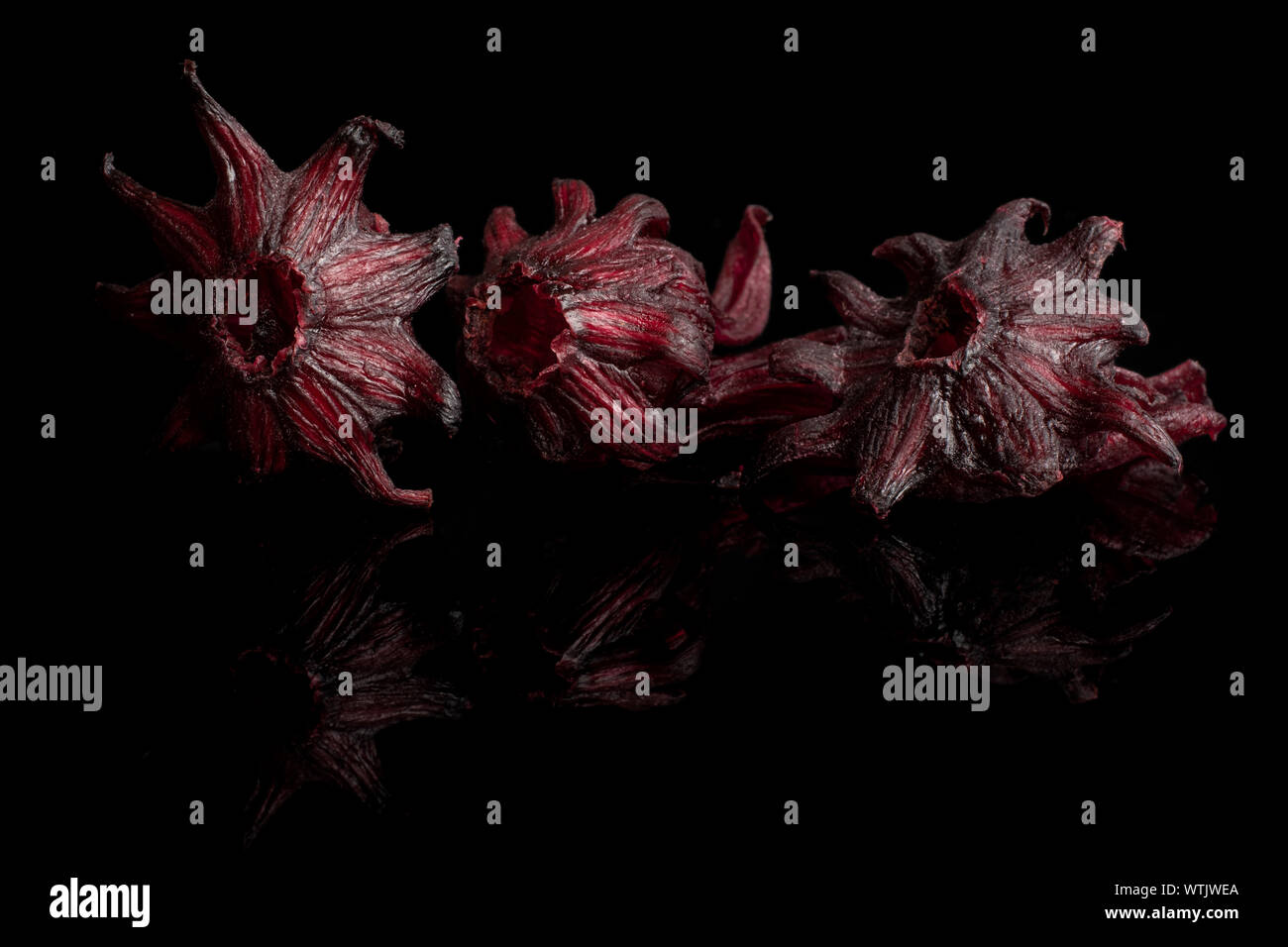 Group of three whole sweet red candied hibiscus isolated on black glass ...