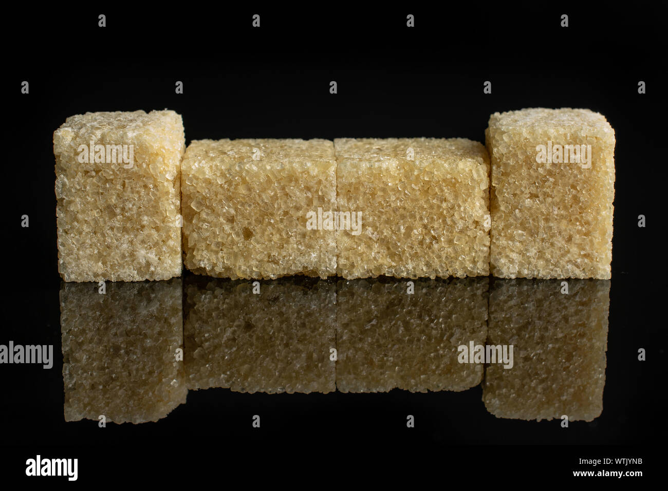 Group of four whole sweet brown sugar cube isolated on black glass ...