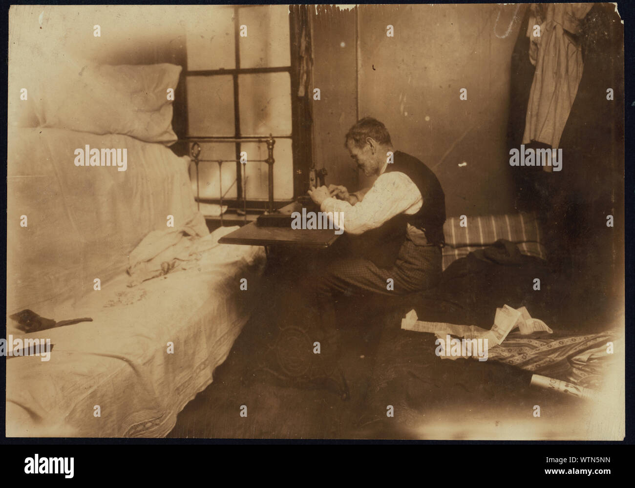Mr. Rothenberg stitching neckties in small inner bed-room. See photo ...