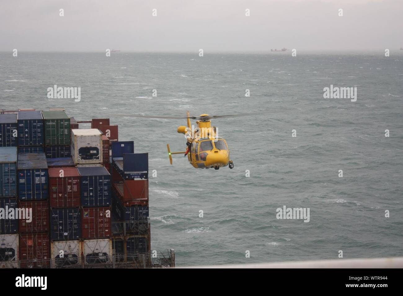 Yellow Helicopter Flying Towards Container Ship On Sea Stock Photo - Alamy