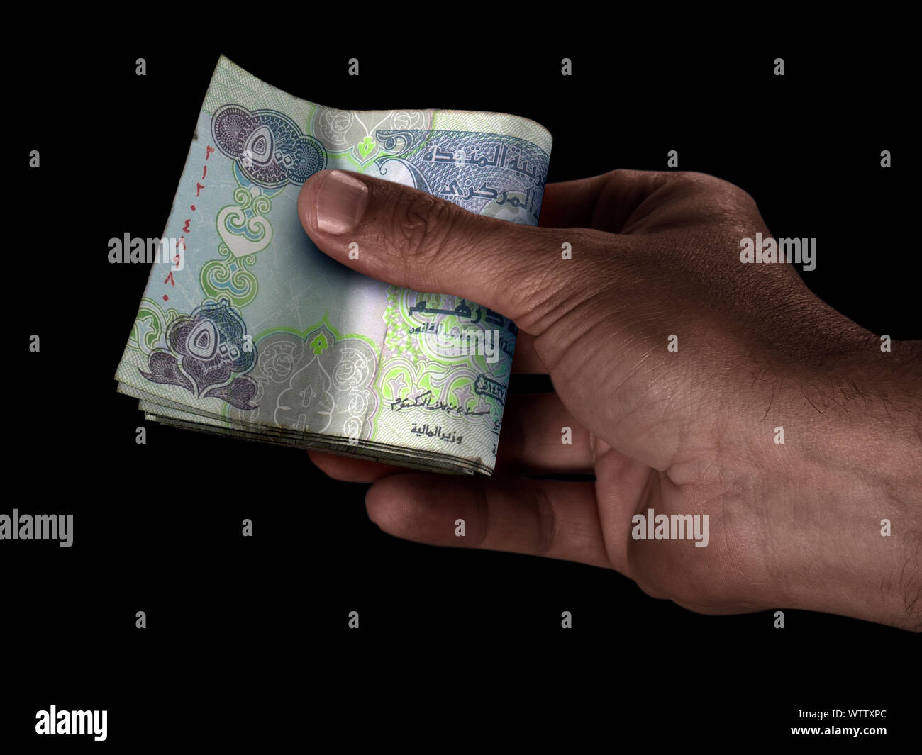 A black male hand handing over a wad of folded dubai dirham bank notes ...