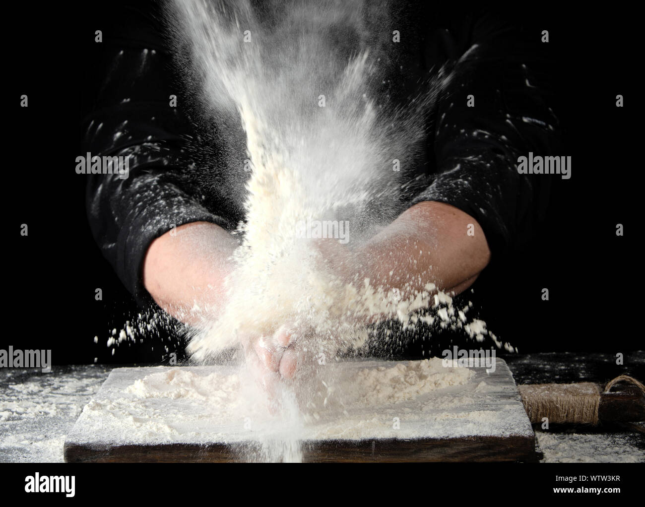 chef in black uniform sprinkles white wheat flour in different ...