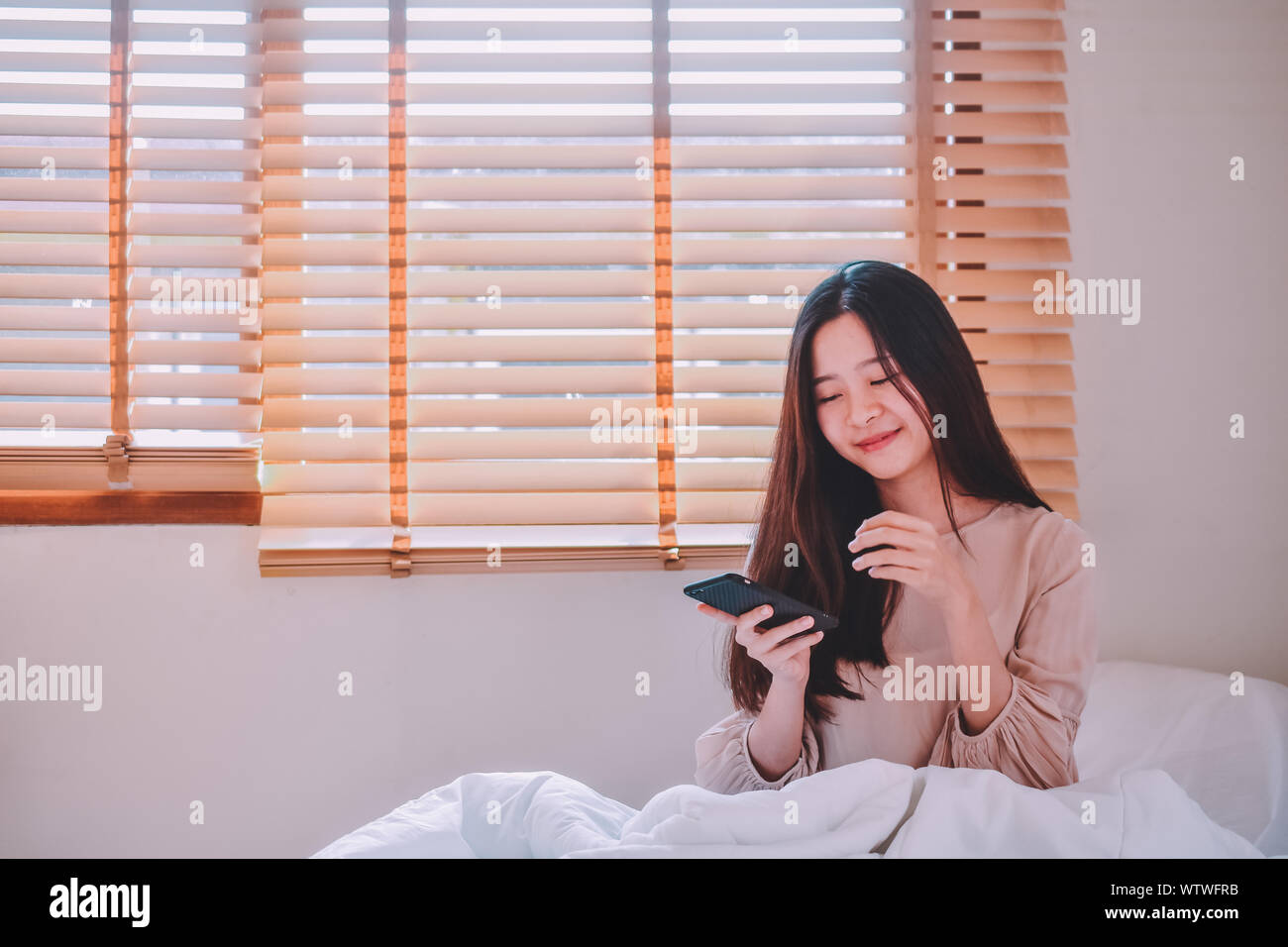 Women holding Mobile smartphone sitting on bed in room Stock Photo - Alamy