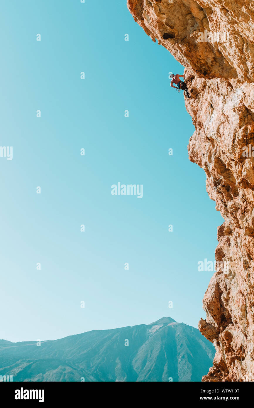 Pulled back view of male climber on wall with El Teide in the back ...