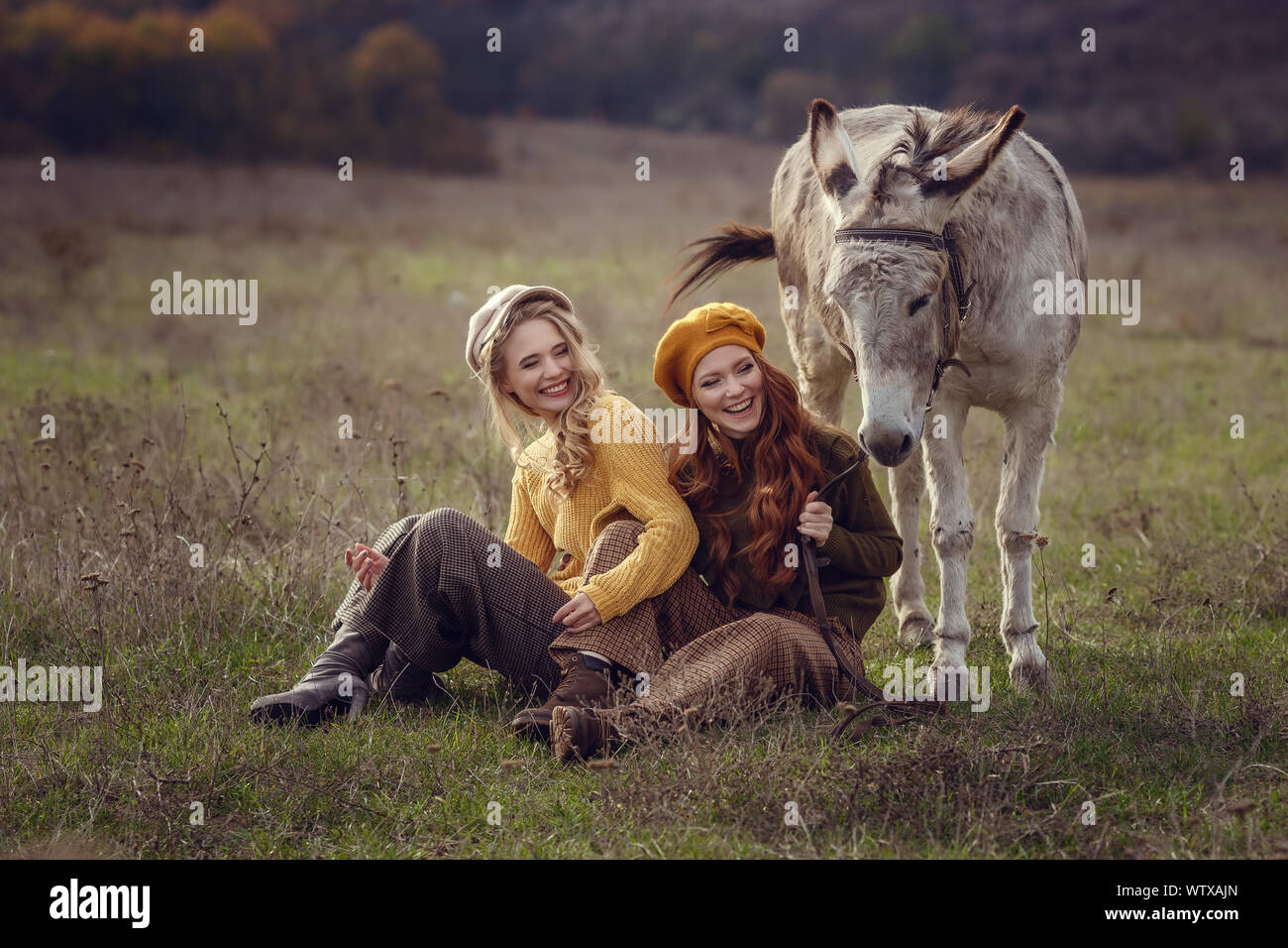 Two charming young women rest on nature together with a cute donkey ...