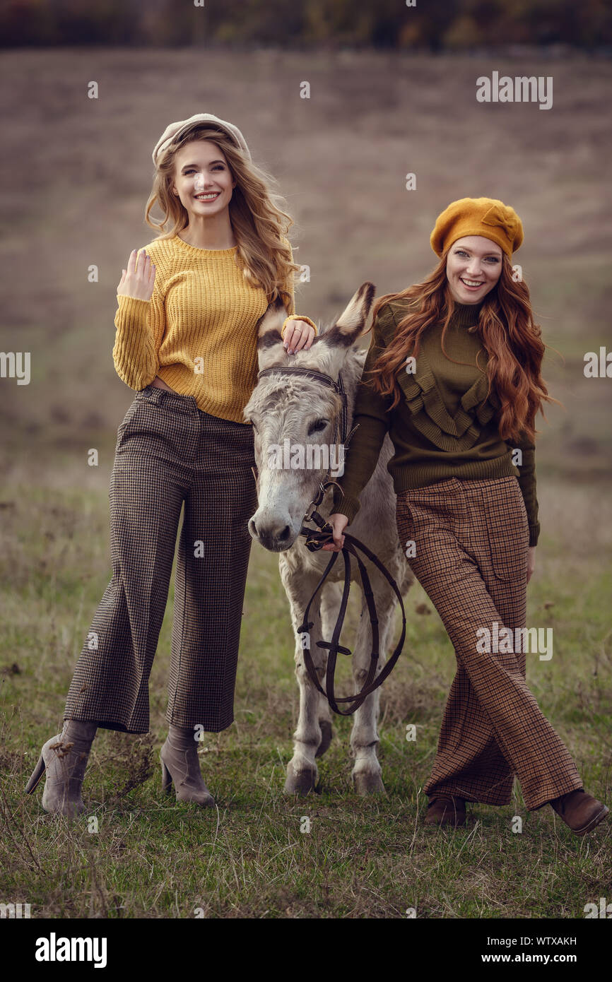 Two charming young women rest on nature together with a cute donkey ...