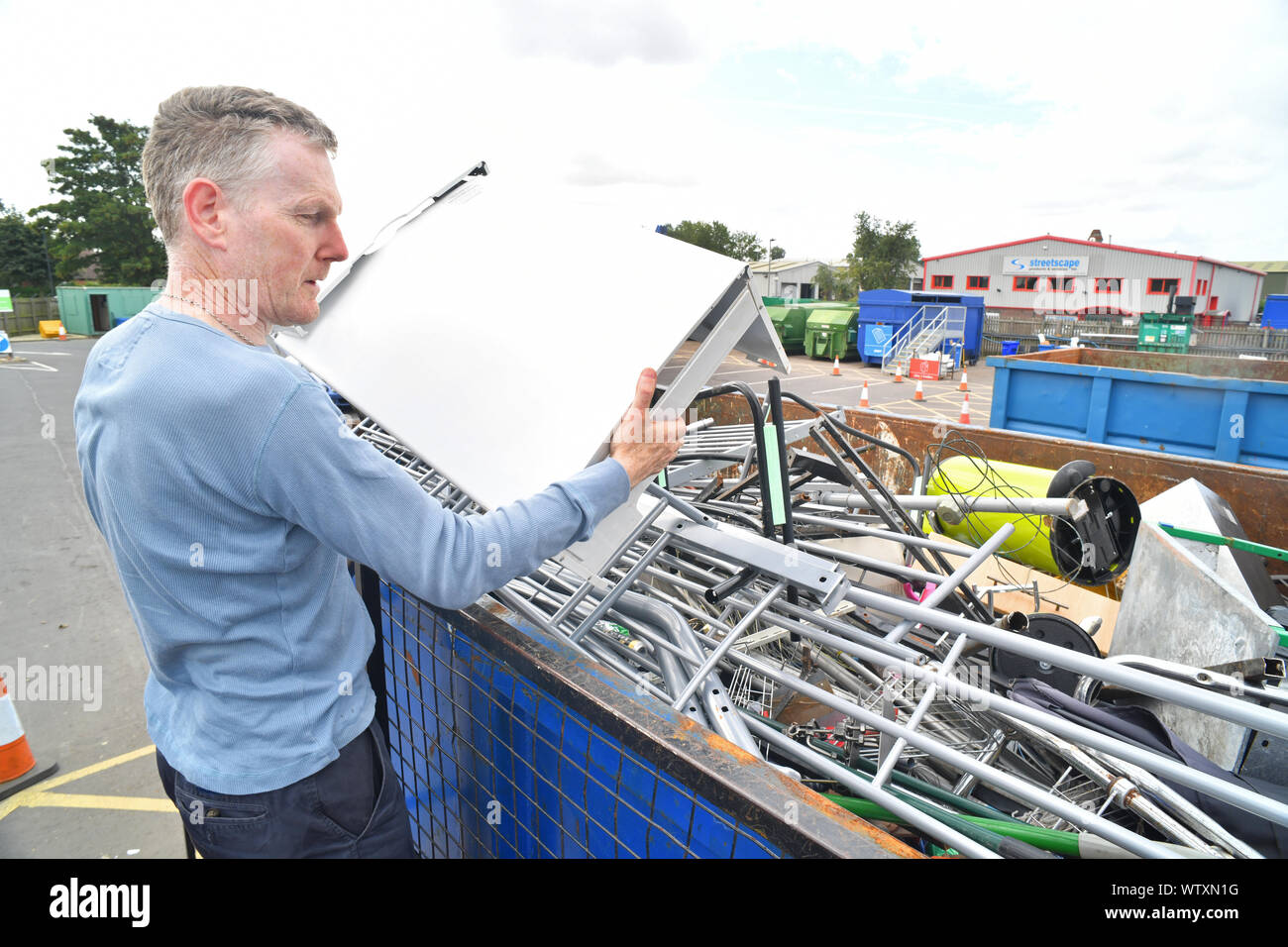 man putting scrap metal into skip for recycling at household waste ...