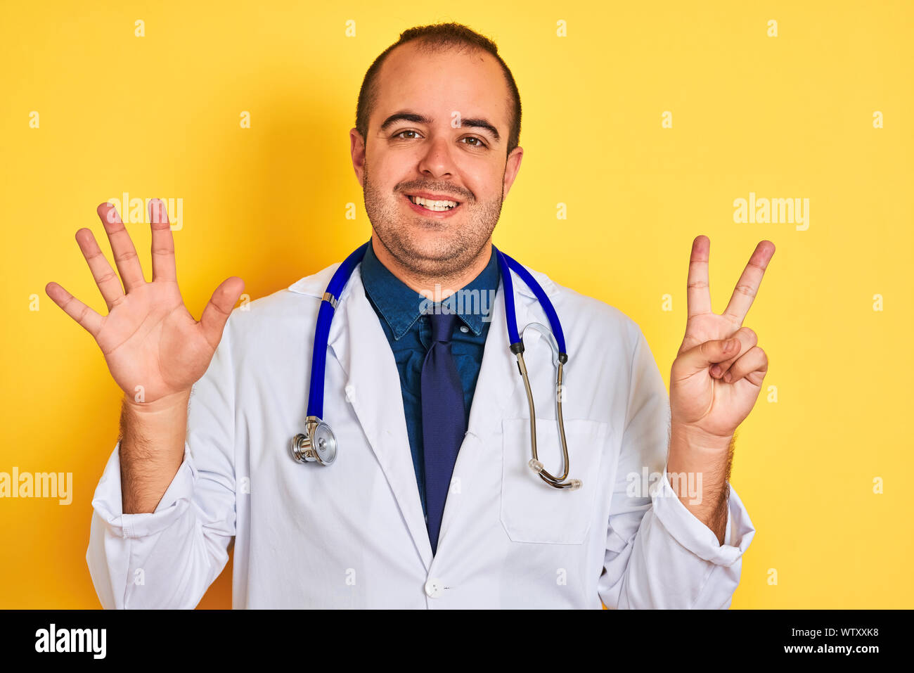 Young doctor man wearing coat and stethoscope standing over isolated ...